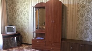 Quarto com guarda-roupa de madeira, uma televisão pequena em um móvel de madeira e papel de parede estampado.