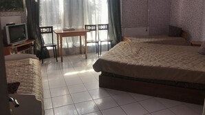 Quarto de hotel com cama, escrivaninha, cadeira, televisão e janela com cortinas.