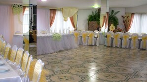Salão de festas com mesas montadas para um evento formal, destacando um piso estampado e cortinas com drapeado.