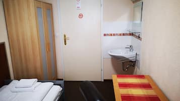 Quarto de hotel com cama, guarda-roupa de madeira, banheiro com pia e espelho, e uma mesa listrada.