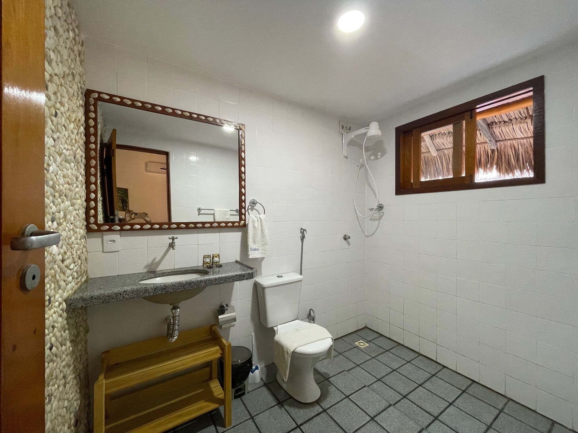 Casa de banho com lavatório de granito, sanita, chuveiro e espelho.