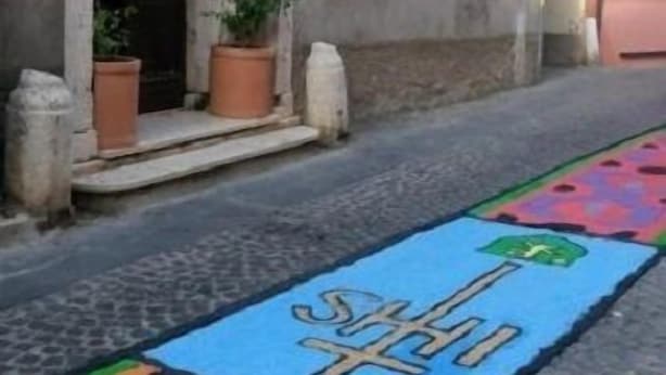 Uma rua com design de calçada colorido e um edifício com arco de pedra e plantas em vasos.