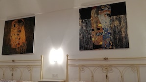 Quarto de hotel com duas camas, uma mesinha de cabeceira e duas pinturas na parede.