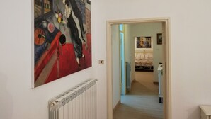 Um corredor com um quadro na parede, um radiador e uma cama ao fundo.