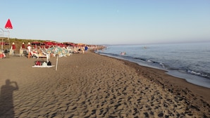 Uma praia com fileiras de guarda-sóis vermelhos e cadeiras de praia, céu claro e mar calmo.