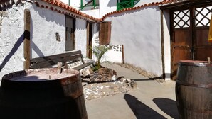Uma estreita viela com paredes brancas, um banco de madeira e um barril rústico.