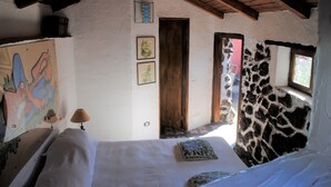 Quarto com cama, luminária, pintura e parede de pedra.
