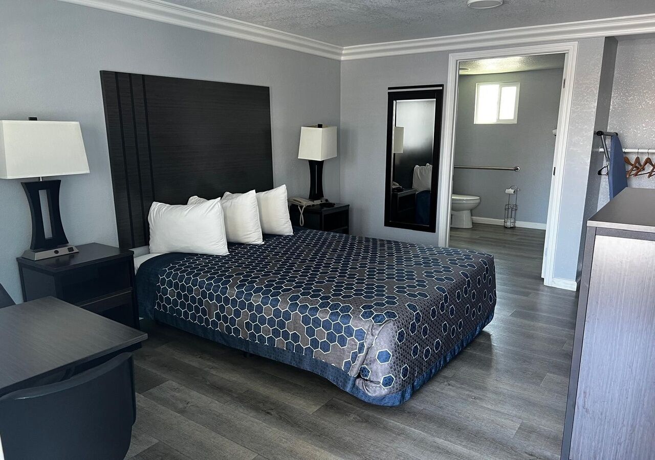 Quarto de hotel com cama, mesas de cabeceira, escrivaninha e banheiro visível através de uma porta aberta.