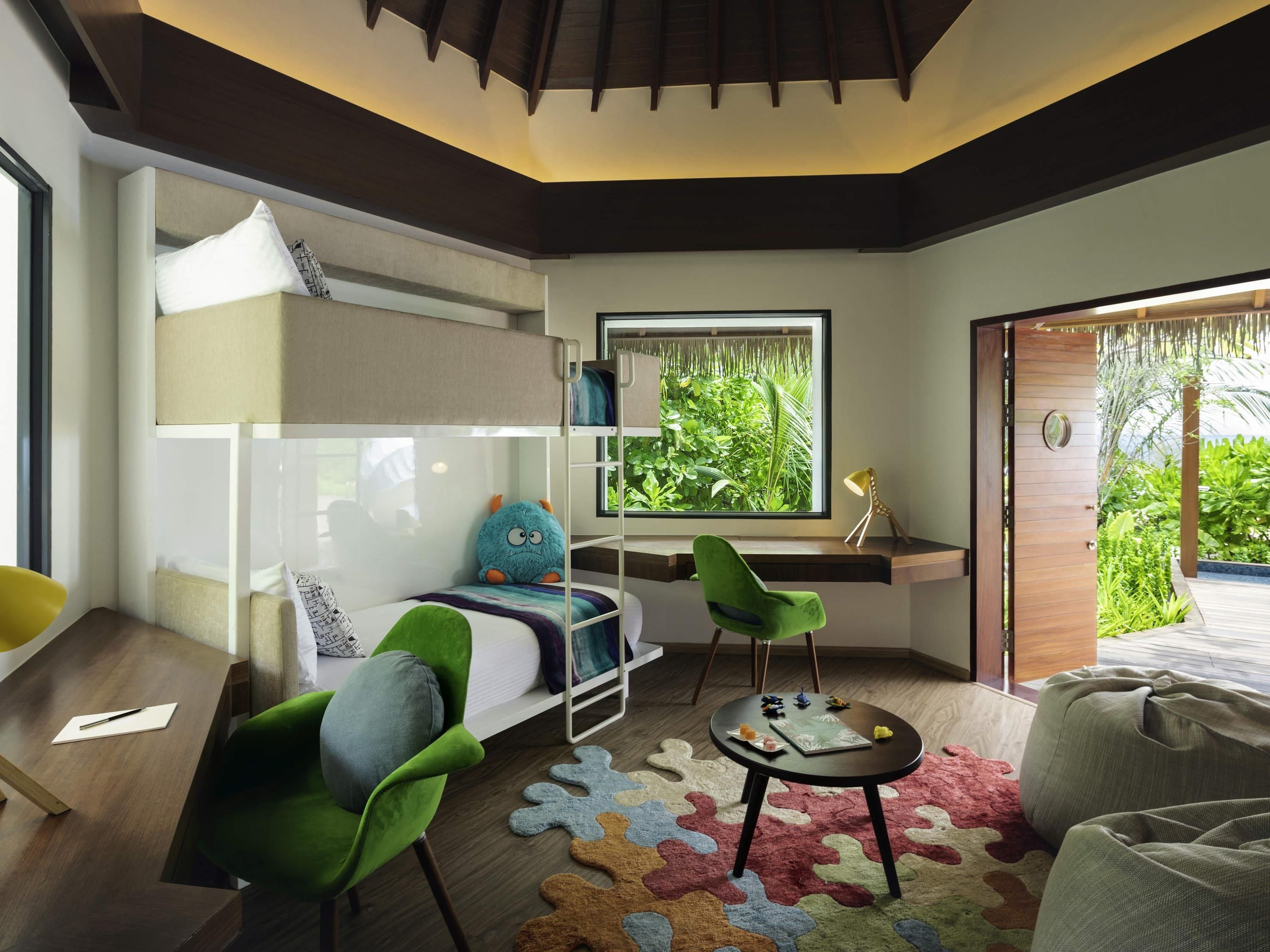 Quarto compacto com beliche, escrivaninha, cadeira e vista para o verde pela janela.