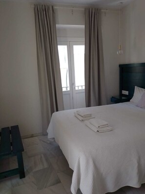 Quarto de hotel com cama, mesa de cabeceira, um banco e vista pela porta.
