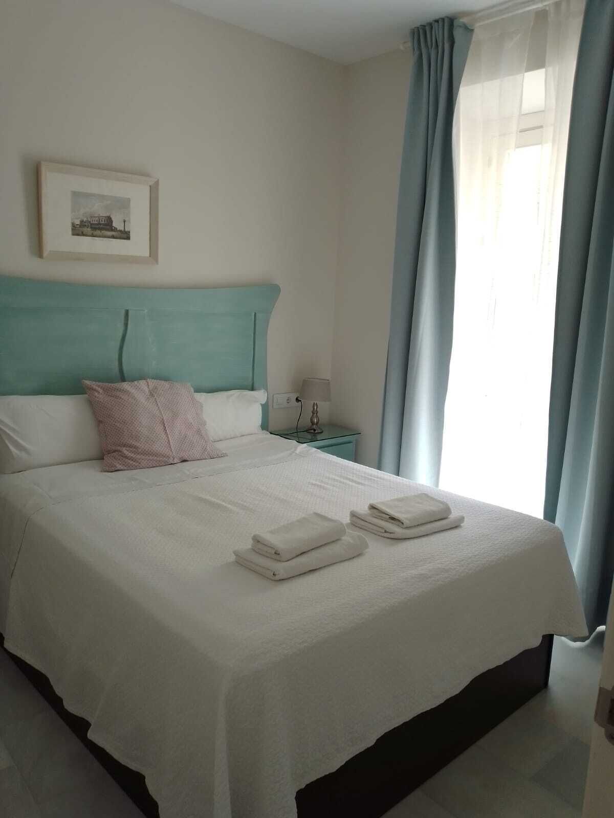 Quarto de hotel com uma cama, mesa de cabeceira, abajur, quadro na parede e janela com cortinas.