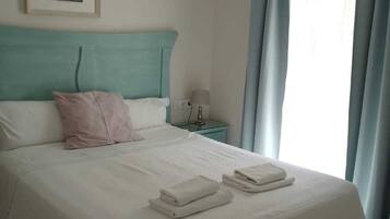 Quarto de hotel com uma cama, mesa de cabeceira, abajur, quadro na parede e janela com cortinas.