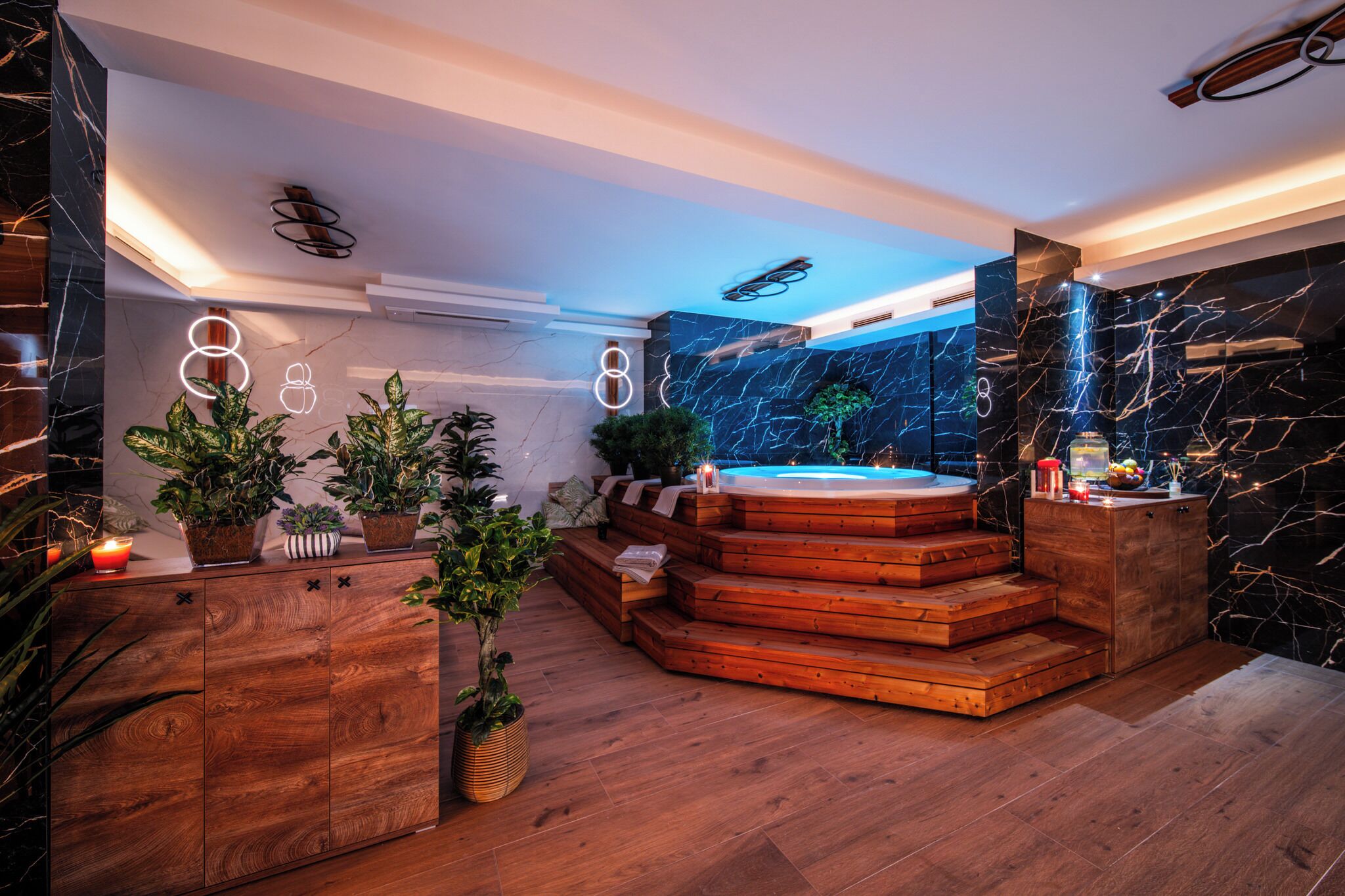 Uma casa de banho moderna com toucador de madeira, parede de mármore, banheira de hidromassagem e plantas em vasos.