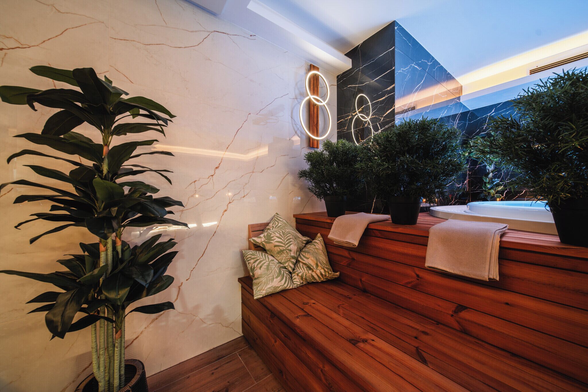 Uma área de spa com um banco de madeira, uma planta grande em vaso e um aplique de parede.