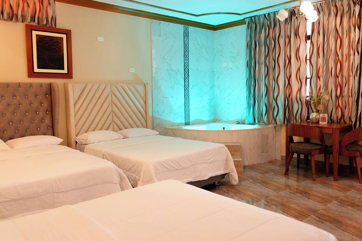 Quarto de hotel com duas camas, área de estar com mesa e cadeiras, e banheira.