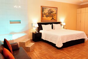 Quarto de hotel com uma cama grande, um espaço de estar com um sofá, um quadro na parede e uma banheira.