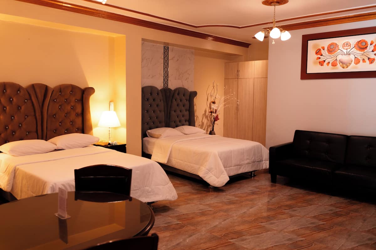 Quarto de hotel com duas camas, um sofá, uma mesa e uma luminária.