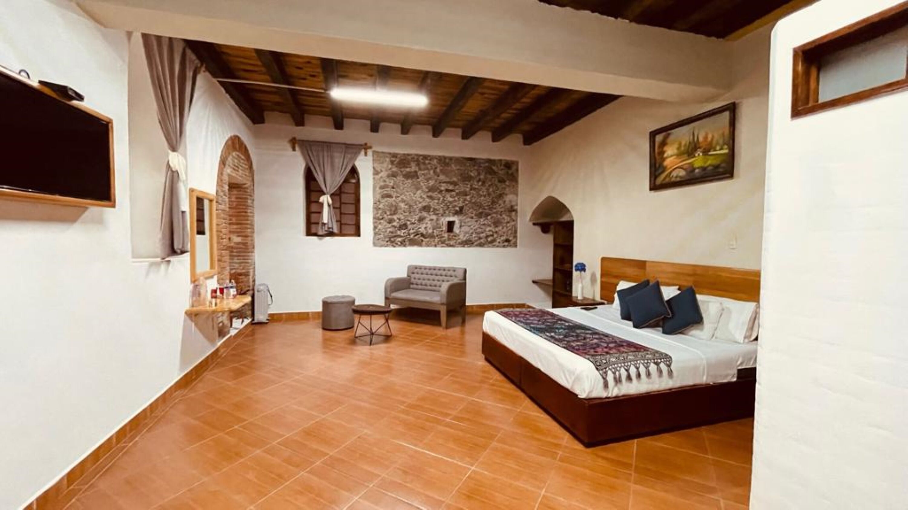 Quarto com cama, cadeira, mesa pequena, televisão e parede de pedra.