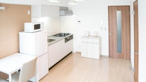 Uma cozinha compacta com micro-ondas, fogão e armários. Há uma mesa de jantar com uma cadeira, e uma porta de madeira com espelho.