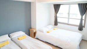 Quarto de hotel com duas camas, uma mesa de cabeceira, uma janela com cortinas e um lustre.