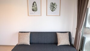 Um sofá cinzento com duas almofadas bege, ladeado por dois quadros com impressões botânicas na parede.