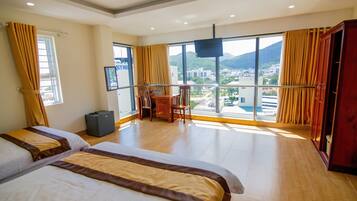 Quarto de hotel com duas camas, uma escrivaninha, uma cadeira, televisão e uma janela grande com vista para a cidade.