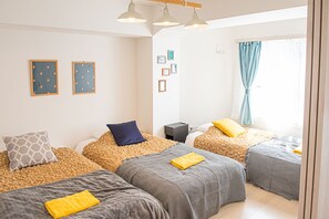 Quarto com duas camas, cada uma com um cobertor cinza e amarelo, e uma mesinha com abajur.