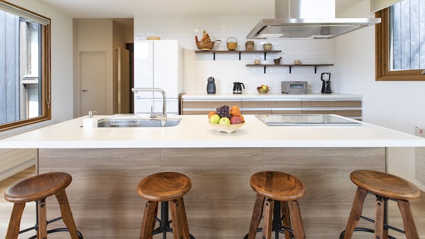 Uma cozinha moderna com uma ilha central, banquetas de bar, uma coifa de aço inoxidável e diversos eletrodomésticos.