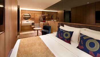 Quarto de hotel com cama, escrivaninha, cadeira, espelho e guarda-roupa.