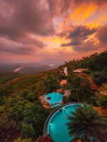 Resort com duas piscinas rodeadas por vegetação exuberante e uma vista panorâmica de um lago e montanhas.