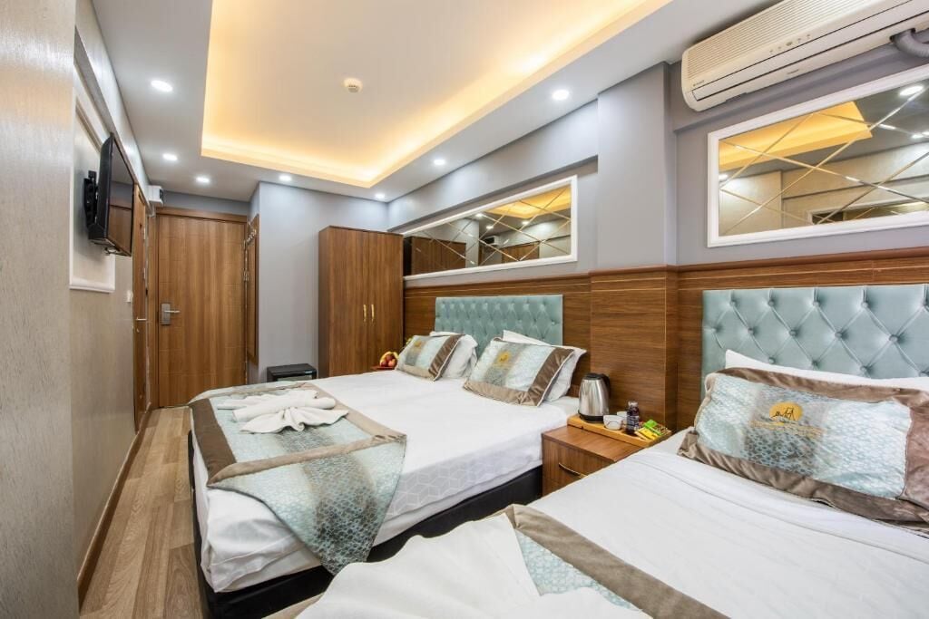 Quarto de hotel com duas camas, um espelho grande, ar condicionado e televisão na parede.