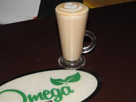 Um copo alto com uma bebida cremosa e arte de latte sobre uma superfície escura.