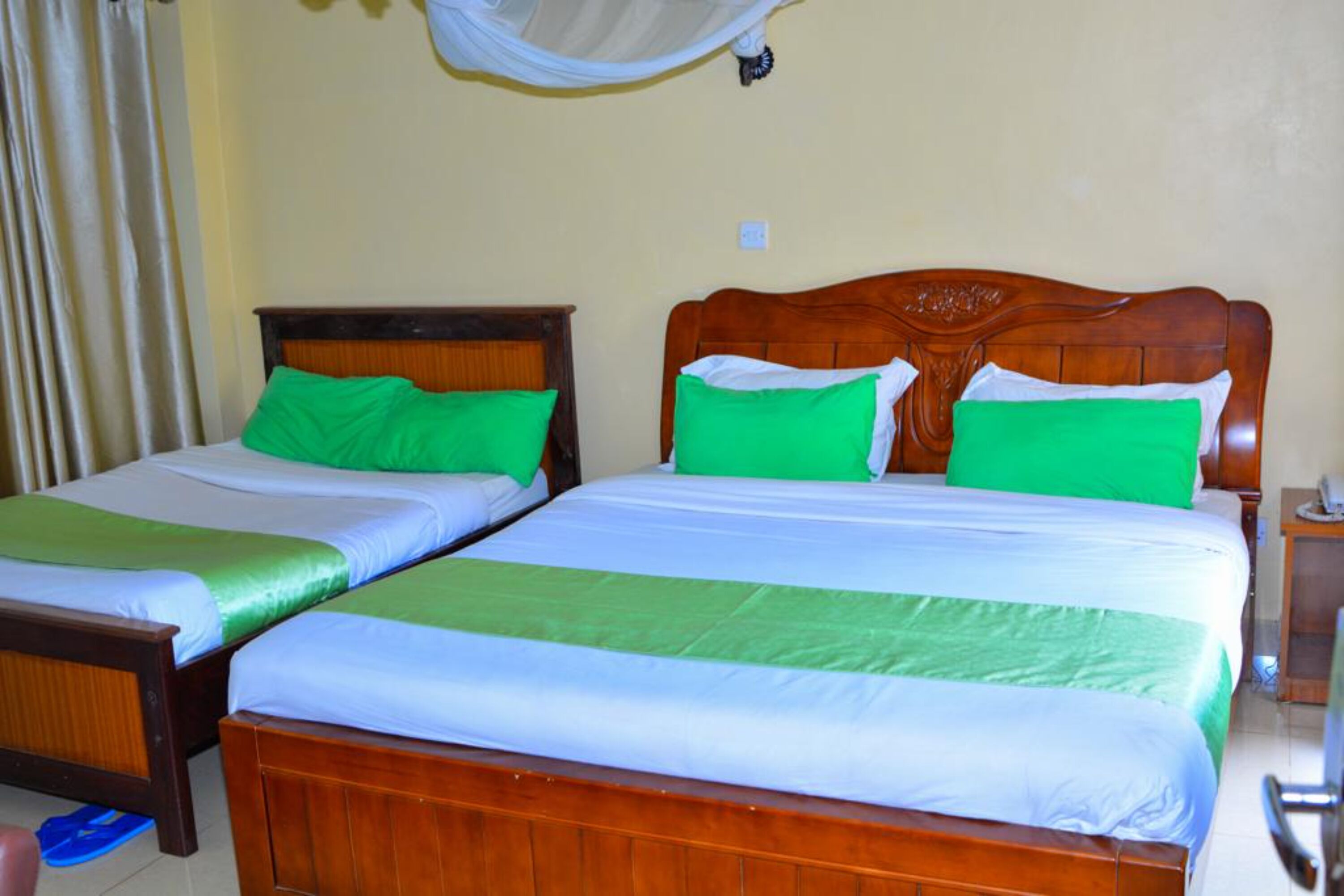 Quarto de hotel com duas camas de madeira, cada uma com roupa de cama verde e branca.
