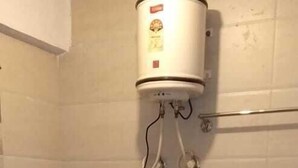 Casa de banho com sanita, chuveiro e termoacumulador fixado na parede.