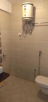 Casa de banho com sanita, chuveiro e termoacumulador fixado na parede.