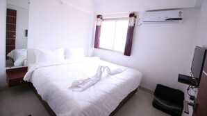 Quarto de hotel com uma cama grande, um espelho, uma janela com cortinas, um aparelho de ar condicionado e uma televisão.