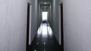 Um corredor longo e estreito com paredes brancas e chão preto, que leva a uma saída iluminada no final.