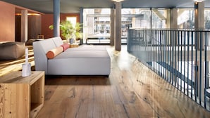 Uma sala de estar moderna com um sofá branco, piso de madeira e grandes janelas com vista para o exterior.