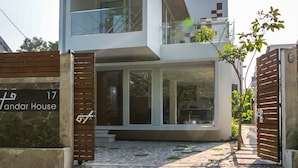 Uma casa moderna de dois andares com escadaria visível, grandes janelas e portão fechado.