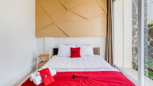 Quarto de hotel moderno com uma cama grande, um edredom listrado em vermelho e branco, um travesseiro vermelho e o logotipo RedDoorz.com.