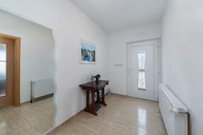 Quarto espaçoso com porta de madeira, radiador, máquina de costura sobre uma mesa e um quadro na parede.