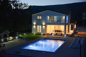 Uma casa moderna de dois andares com piscina, área de estar externa e um pátio bem iluminado.