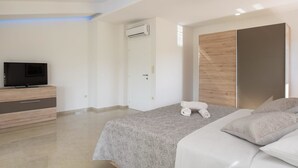 Quarto moderno com cama, TV em penteadeira de madeira e ar condicionado na parede.