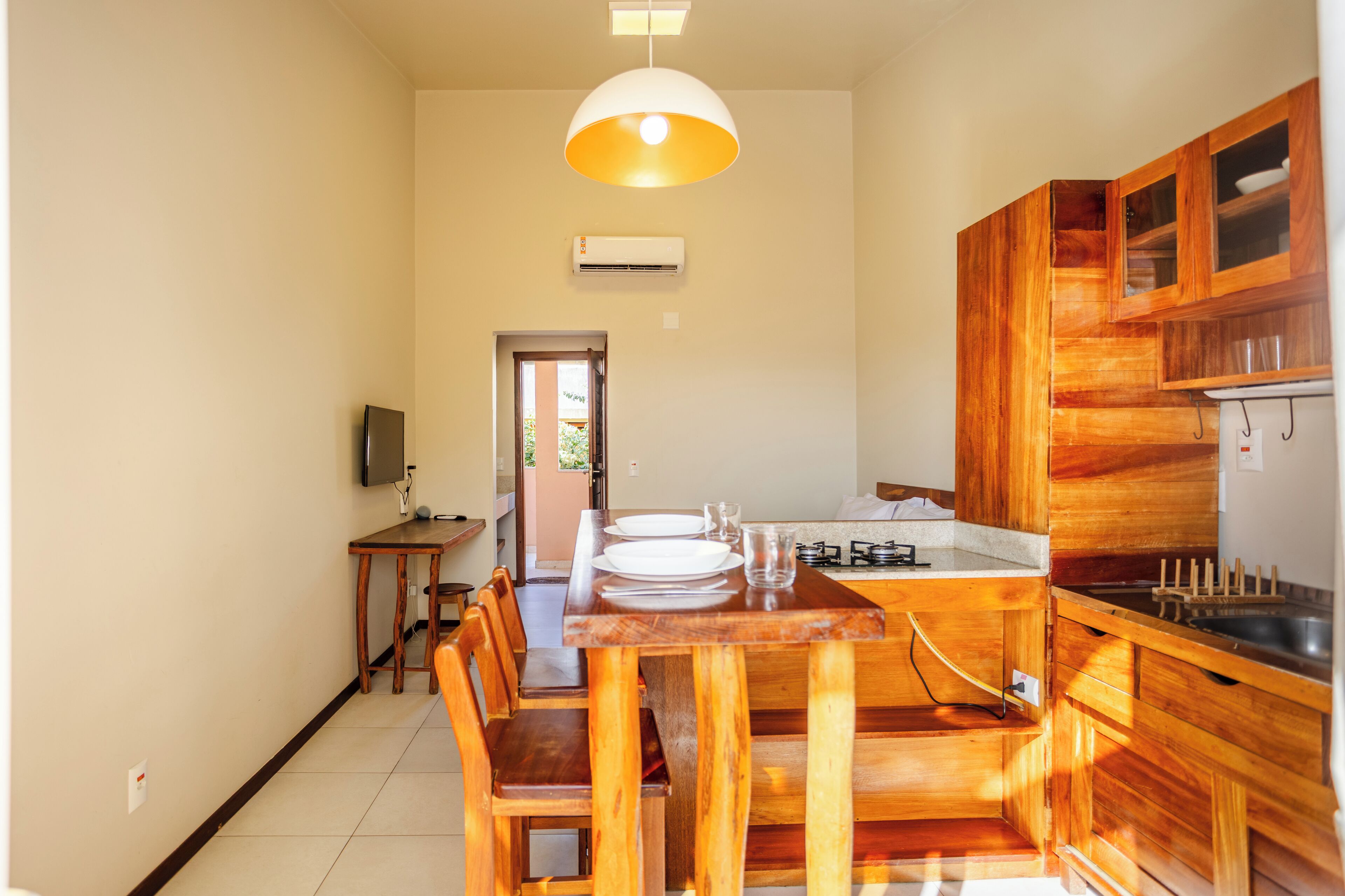 Uma mesa de jantar de madeira com cadeiras, uma luminária pendente e uma cozinha com armários de madeira e um fogão.