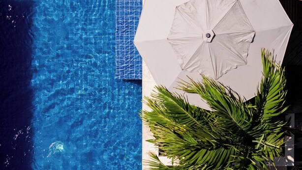 Vista aérea de uma piscina com laterais em azulejo, rodeada por um deck de madeira e espreguiçadeiras.