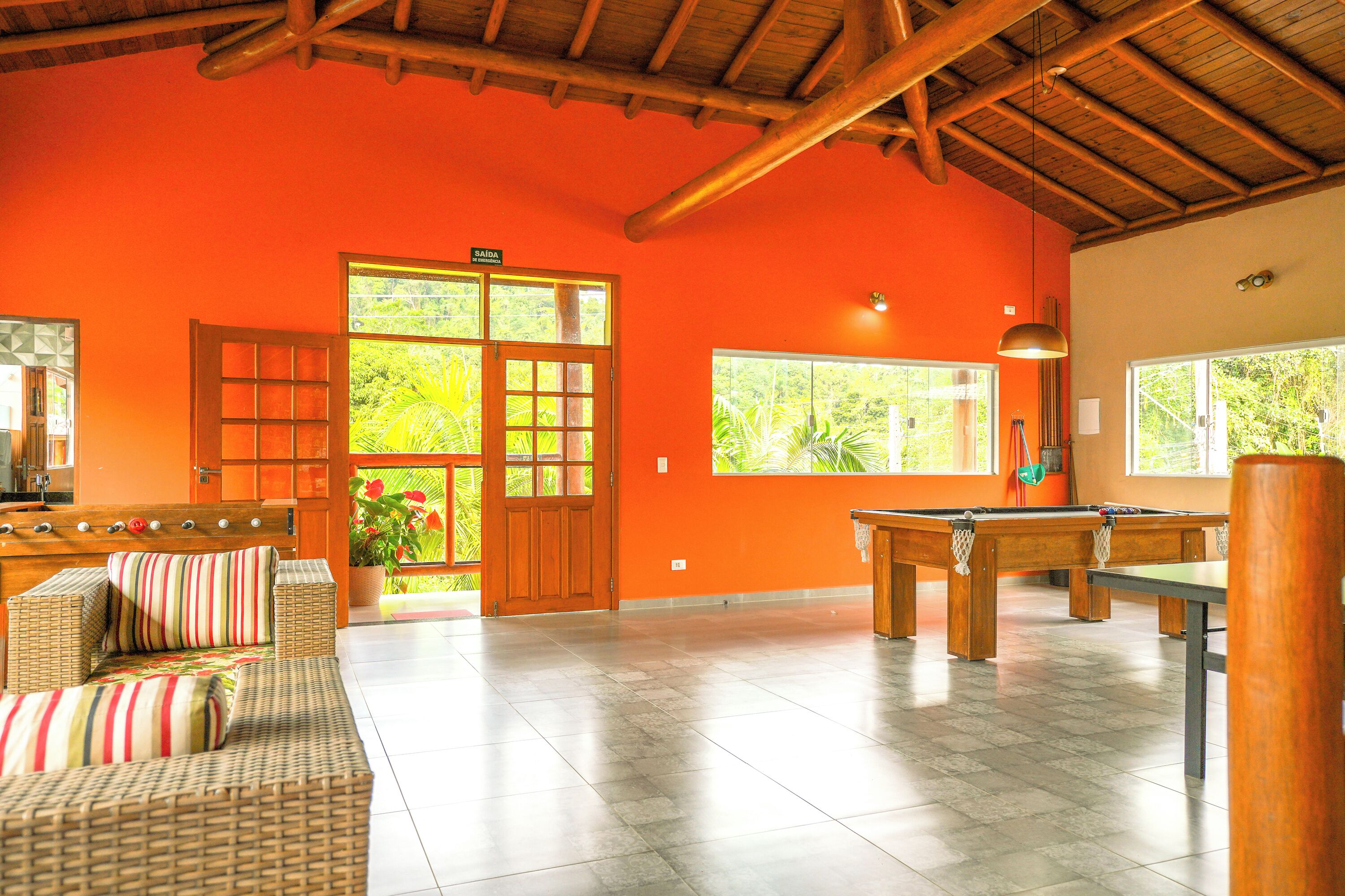 Uma sala iluminada, com mesa de bilhar, sofá e porta que dá para o exterior.