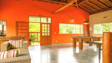 Uma sala iluminada, com mesa de bilhar, sofá e porta que dá para o exterior.