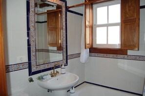 Casa de banho com lavatório branco, espelho e armários de madeira.