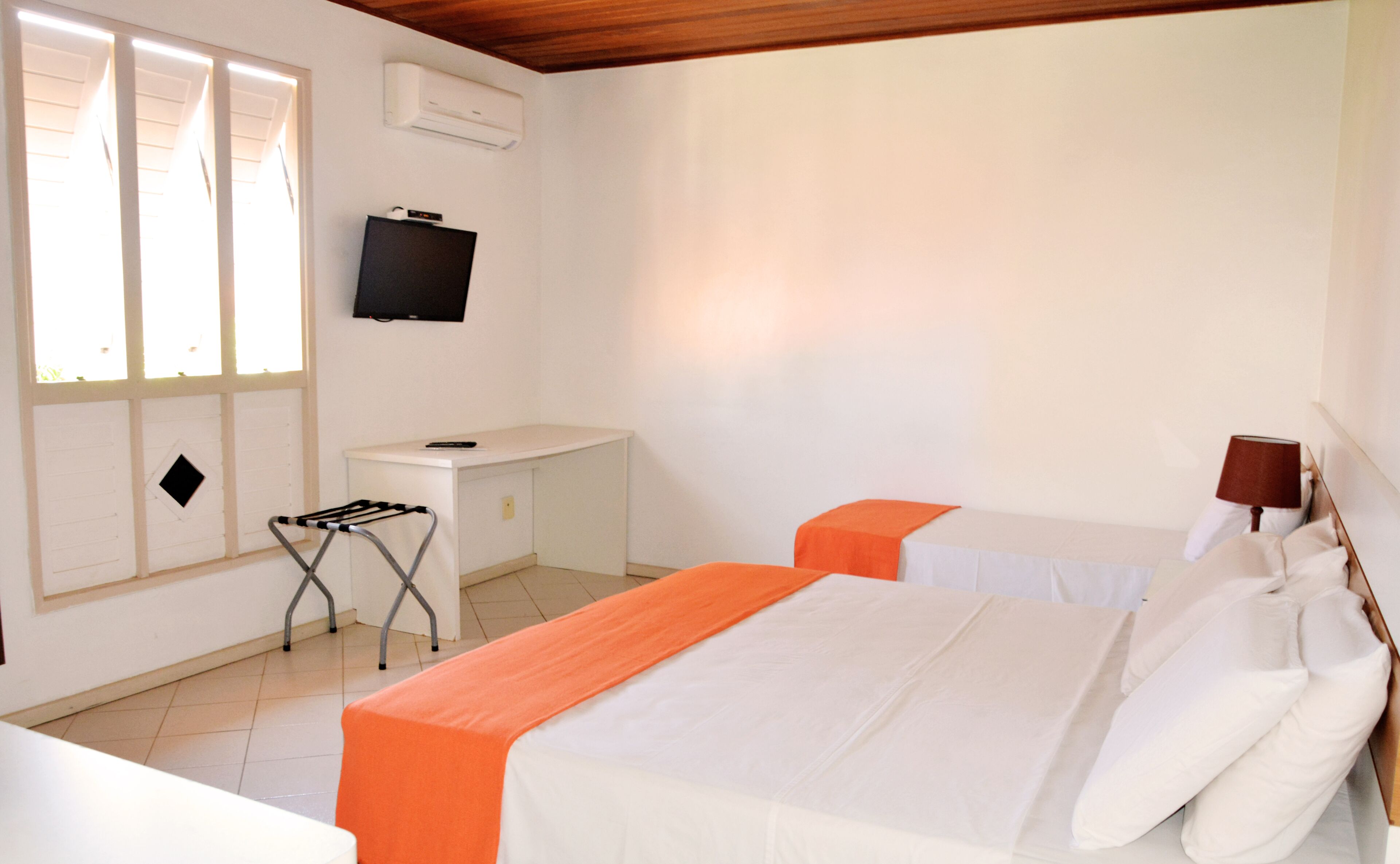 Quarto de hotel com cama, secretária e televisão.