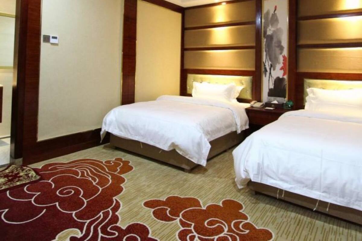 Quarto de hotel com duas camas, um espelho grande, um painel decorativo na parede e um tapete com padrão floral.